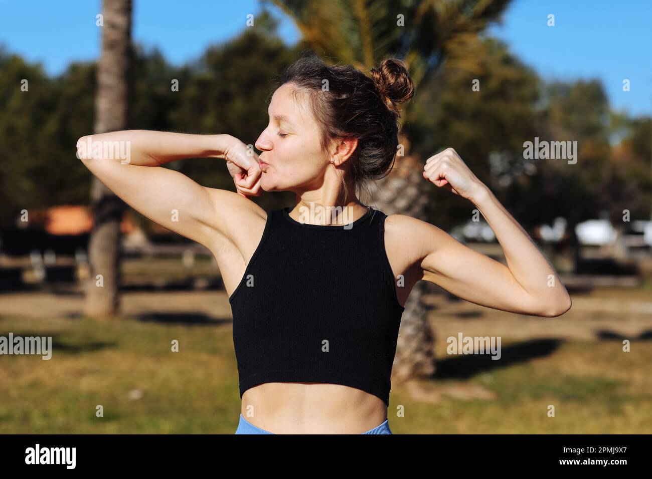 Young beautiful woman in sportswear raises arms to show muscles, biceps ...