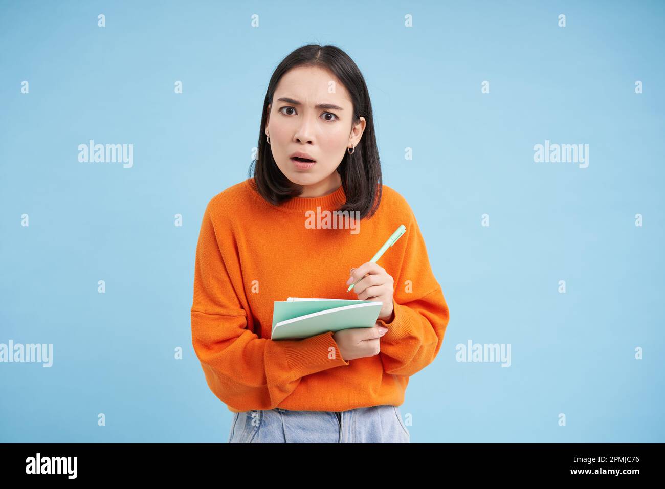 Portrait of confused asian girl, taking notes and looking puzzled while ...