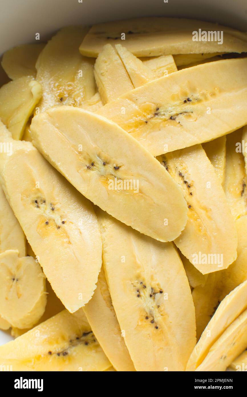 slices of ripe plantains in a white bowl, slices of yellow plantains ...