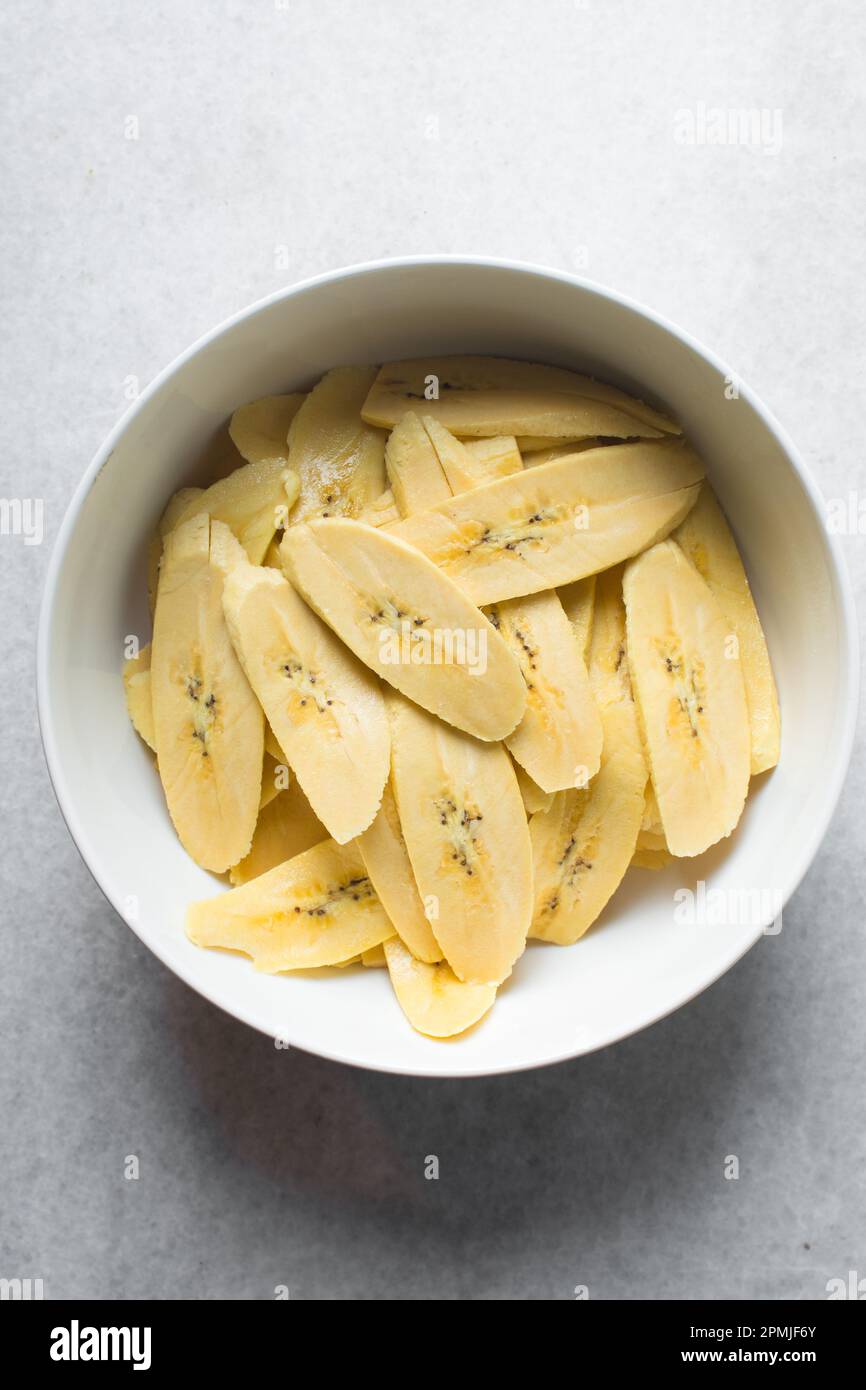slices of ripe plantains in a white bowl, slices of yellow plantains ...