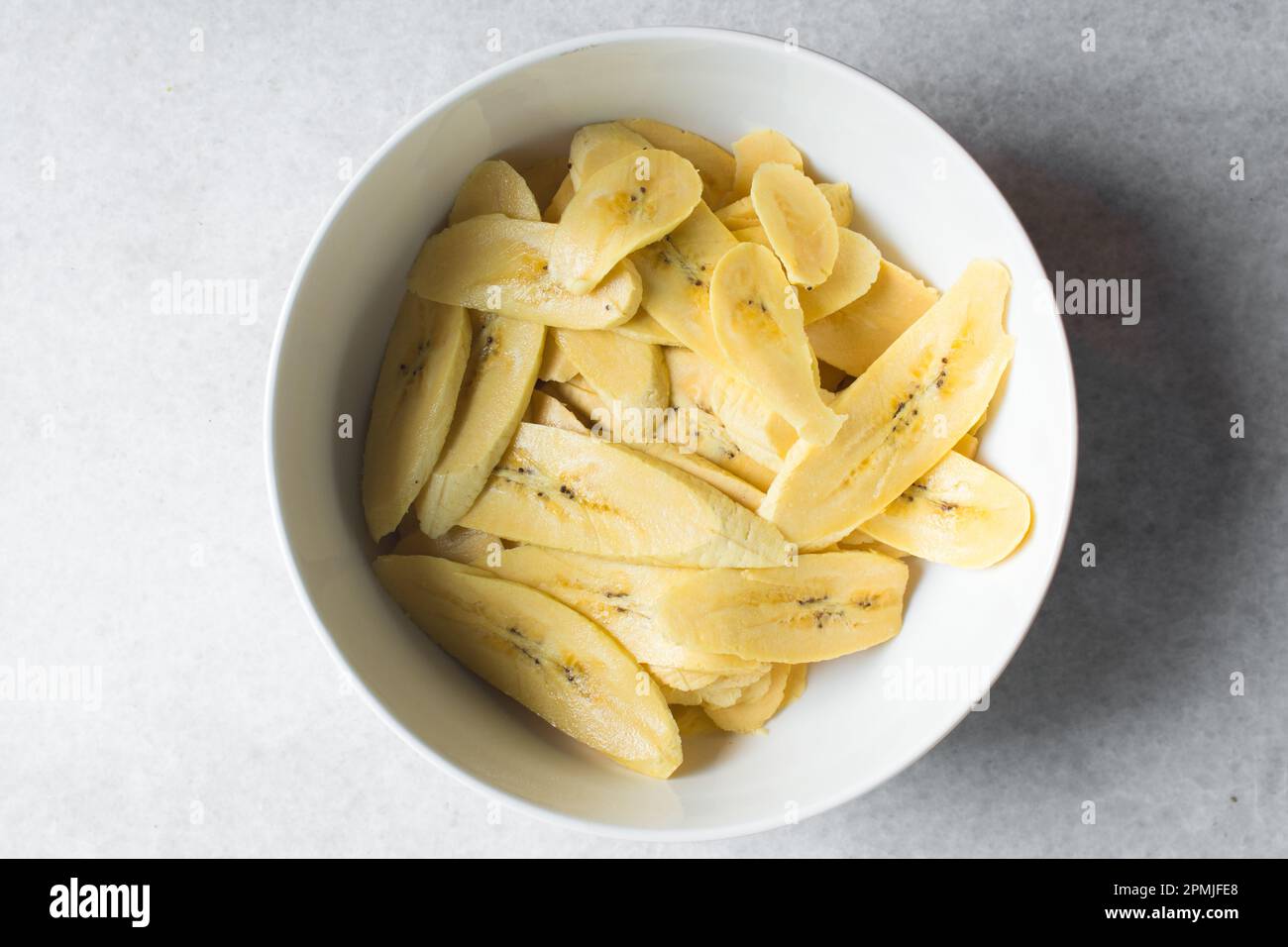 slices of ripe plantains in a white bowl, slices of yellow plantains ...