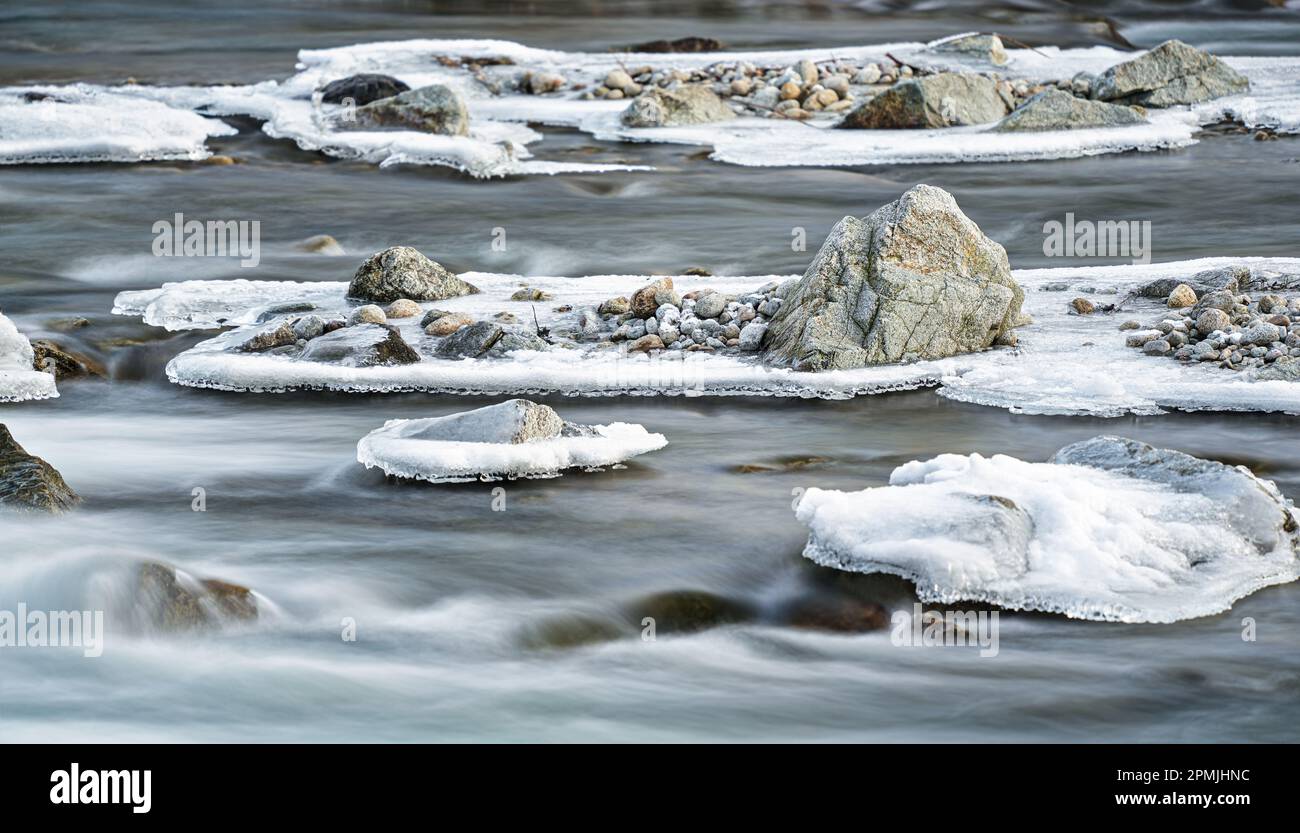 Winter river flowing around snow and ice covered rocks, long exposure ...