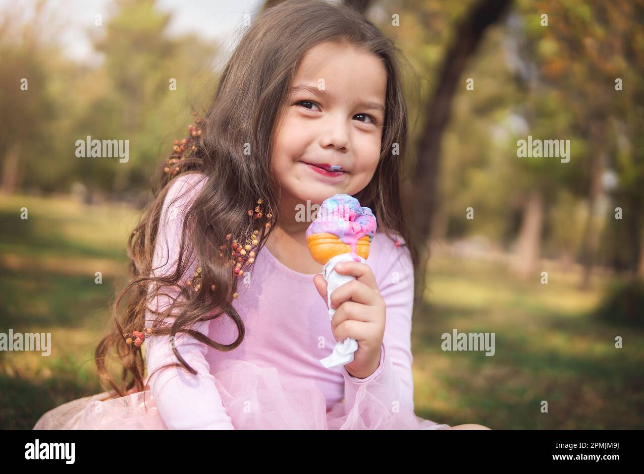 Cute blonde curly haired girl eating a nice ice cream in the forest on a nice summer day, she ...