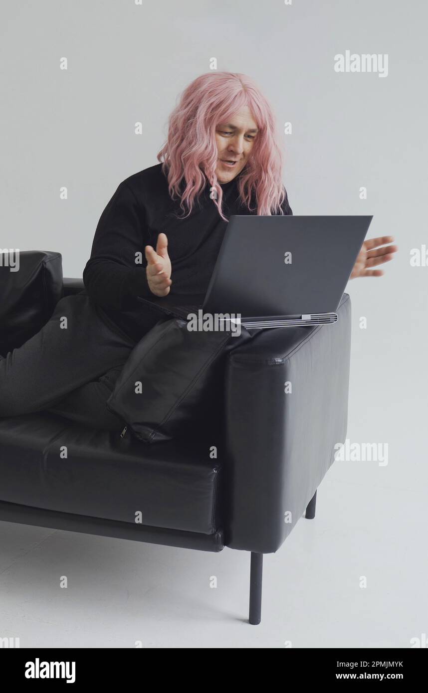 Portrait of a smiling man in a pink wig, sits on a sofa, communicates ...