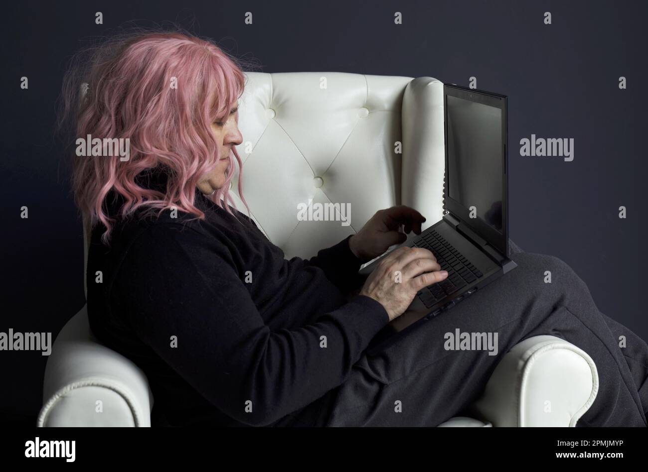 A man in a pink wig sits in a white chair and works at a computer Stock ...