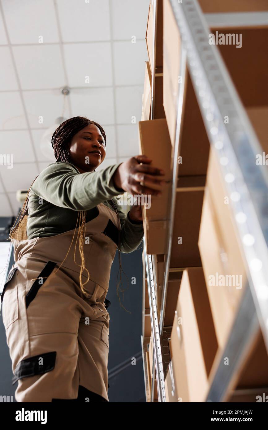 Stockroom employee taking out cardboard box from metallic shelf ...