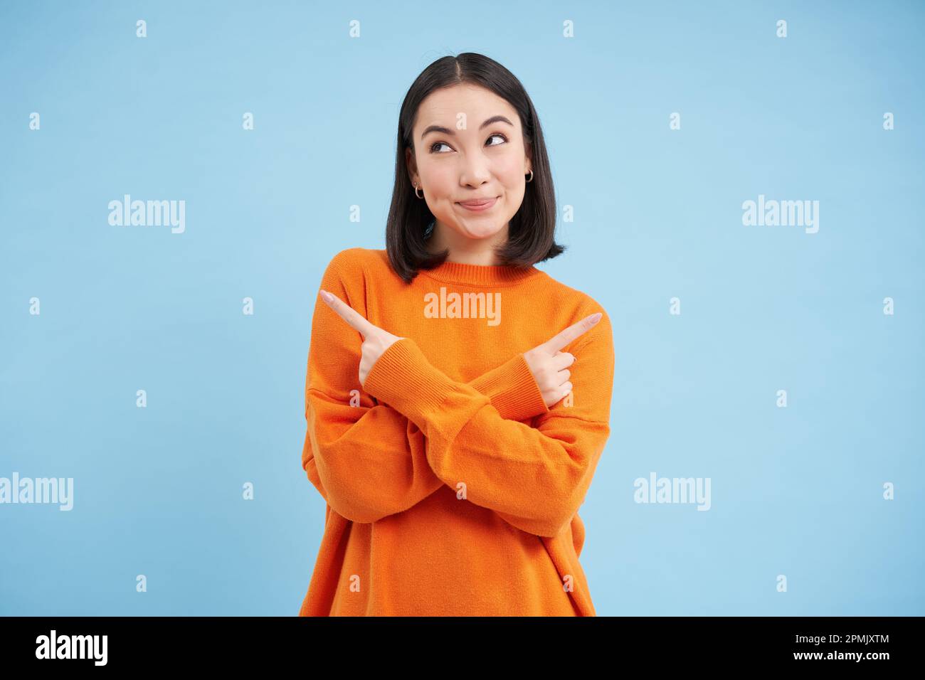 Decisions. Young asian woman points sideways, shows left and right with ...
