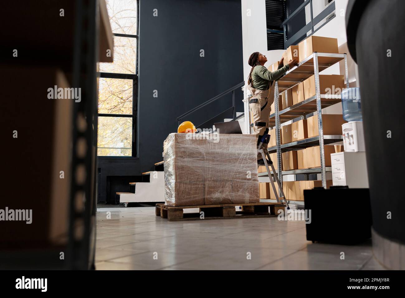 Storehouse worker taking out cardboard box from metallic shelf, working ...