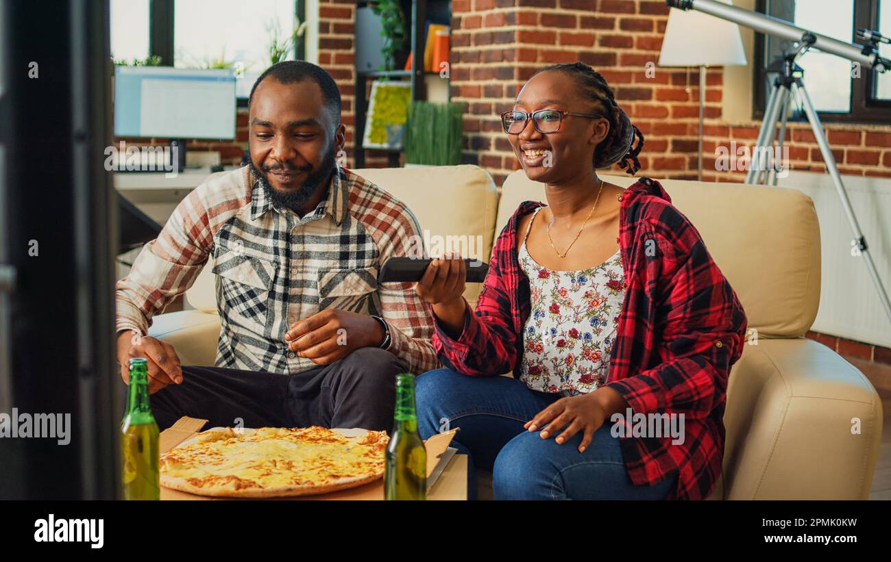 Boyfriend and girlfriend enjoying pizza slices and binge watching show ...
