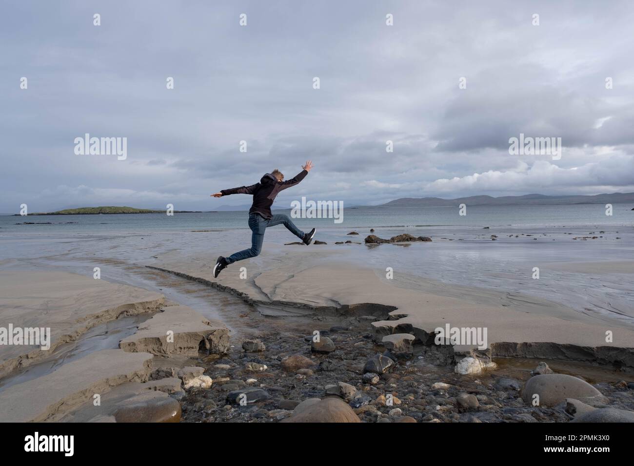A person jumping over a tiny stream on a beach Stock Photo - Alamy