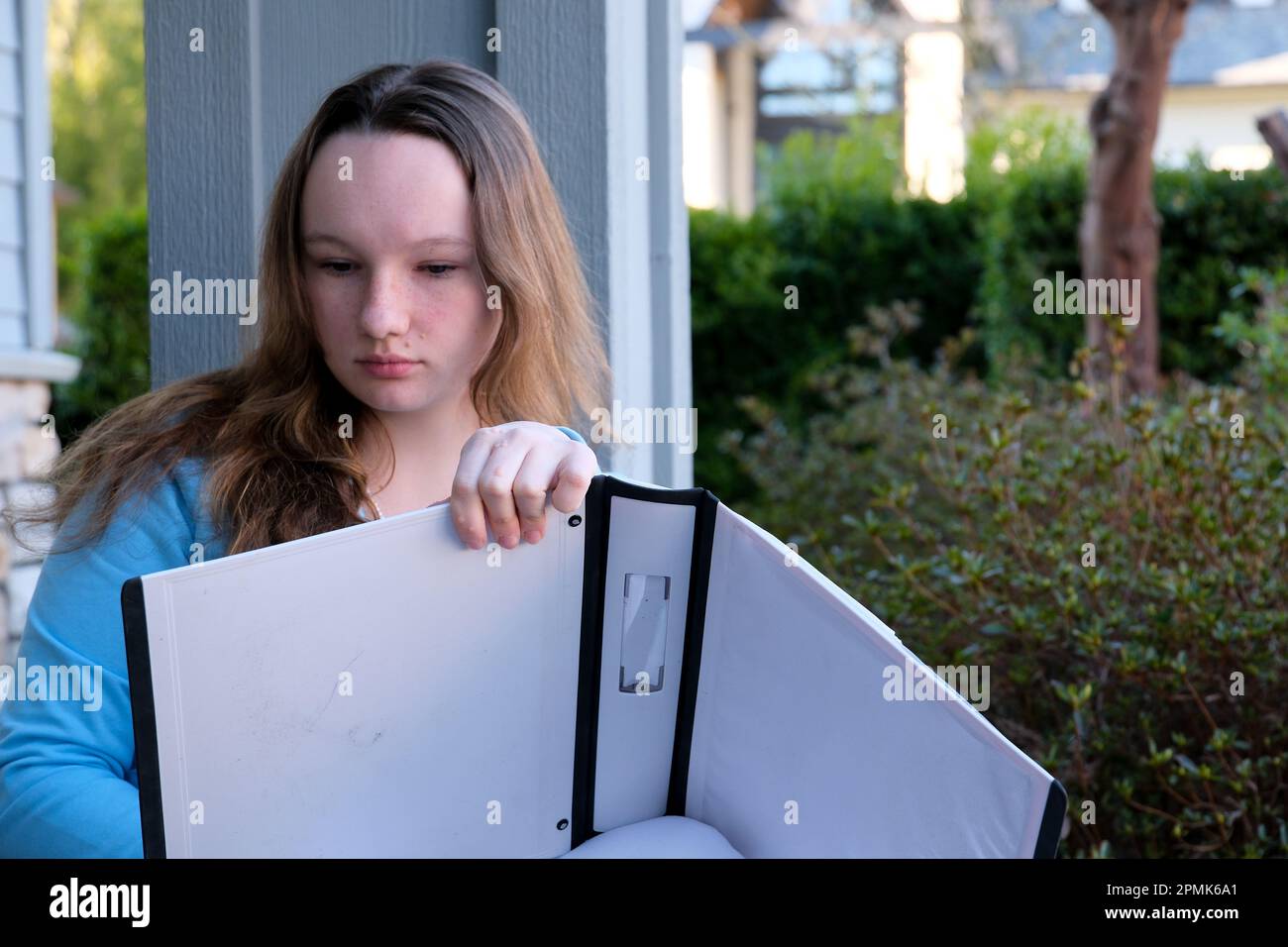 teenage girl with big white folder in hands crosses out something with ...