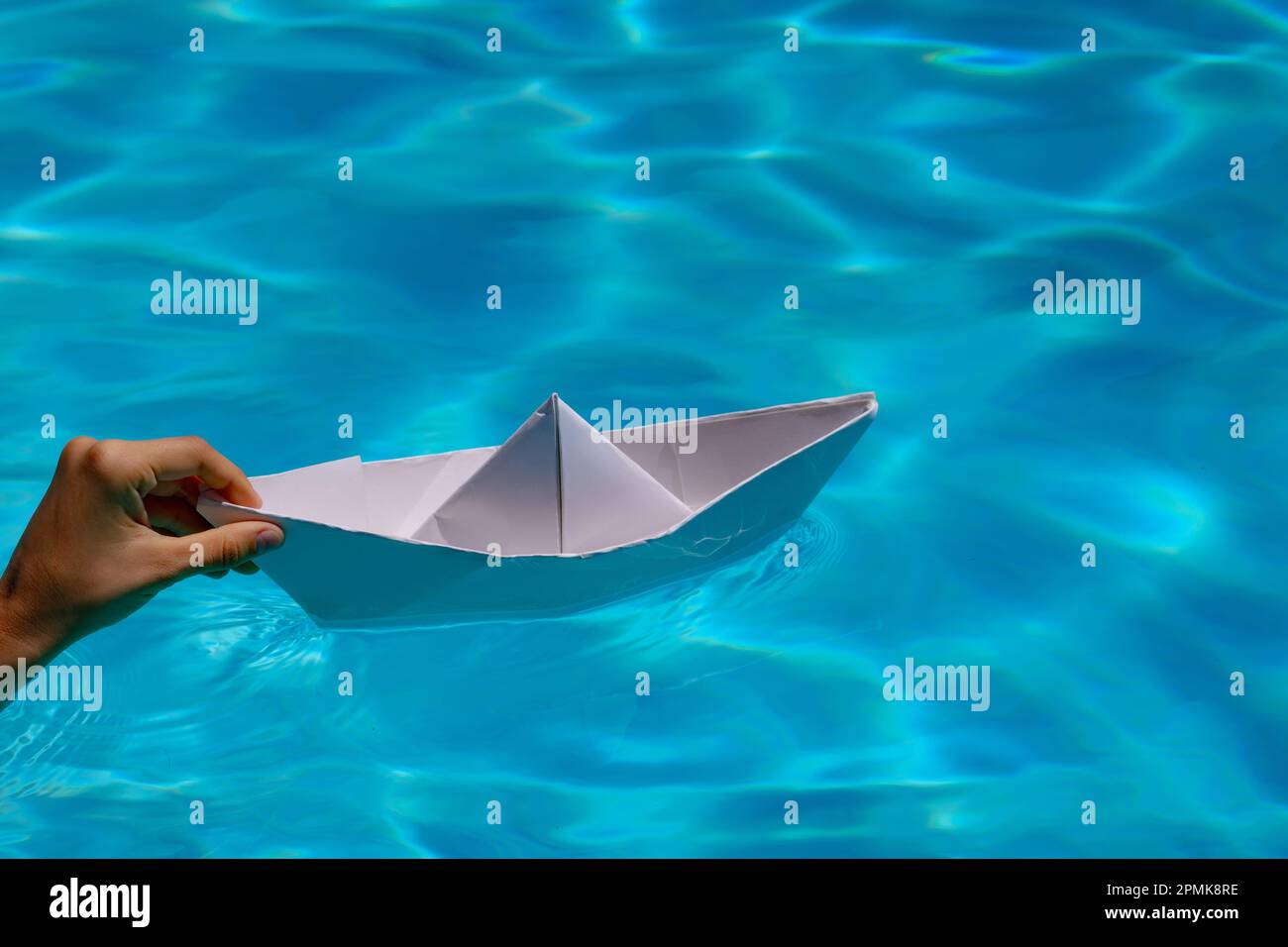 Hand is launching a white paper boat into the clear sea water Stock ...