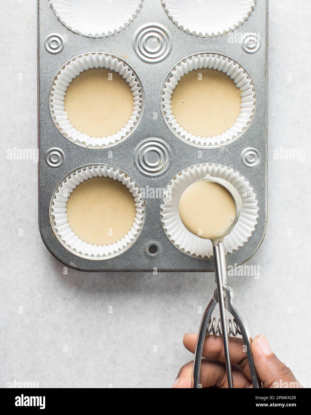 Hand scooping vanilla cake batter into a cupcake tin, An ice cream ...