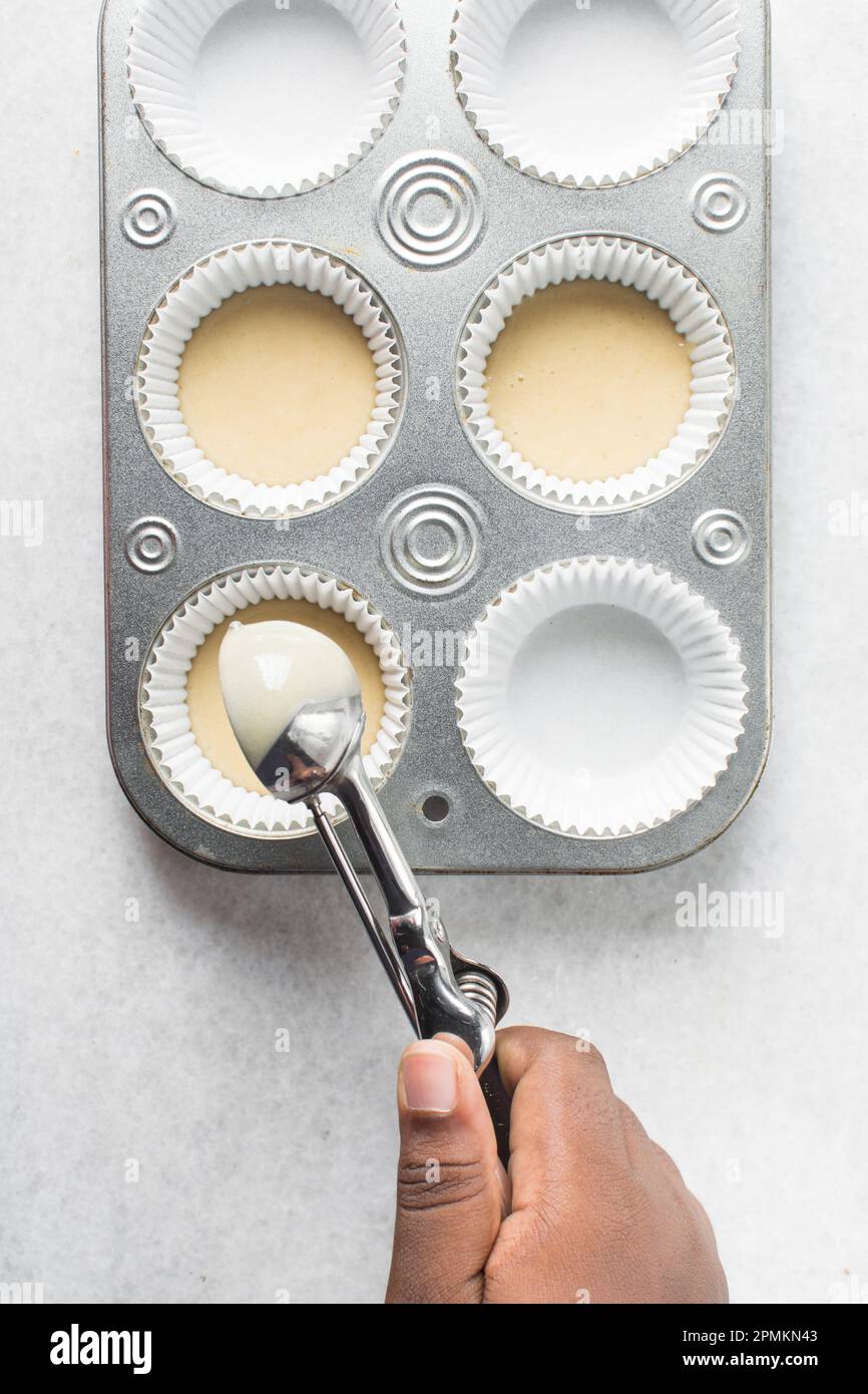 Hand scooping vanilla cake batter into a cupcake tin, An ice cream ...