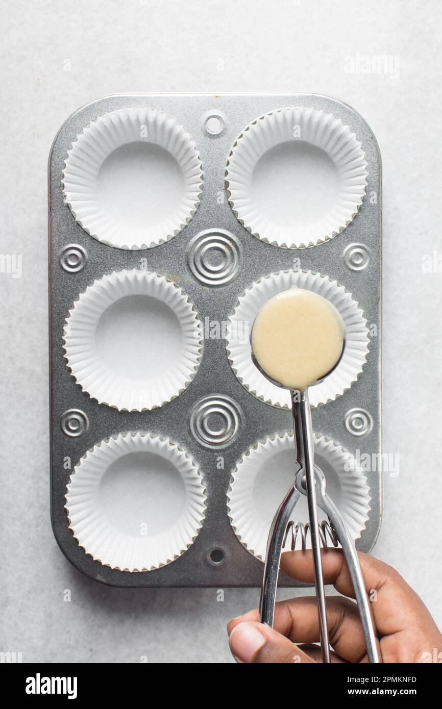 Hand scooping vanilla cake batter into a cupcake tin, An ice cream ...