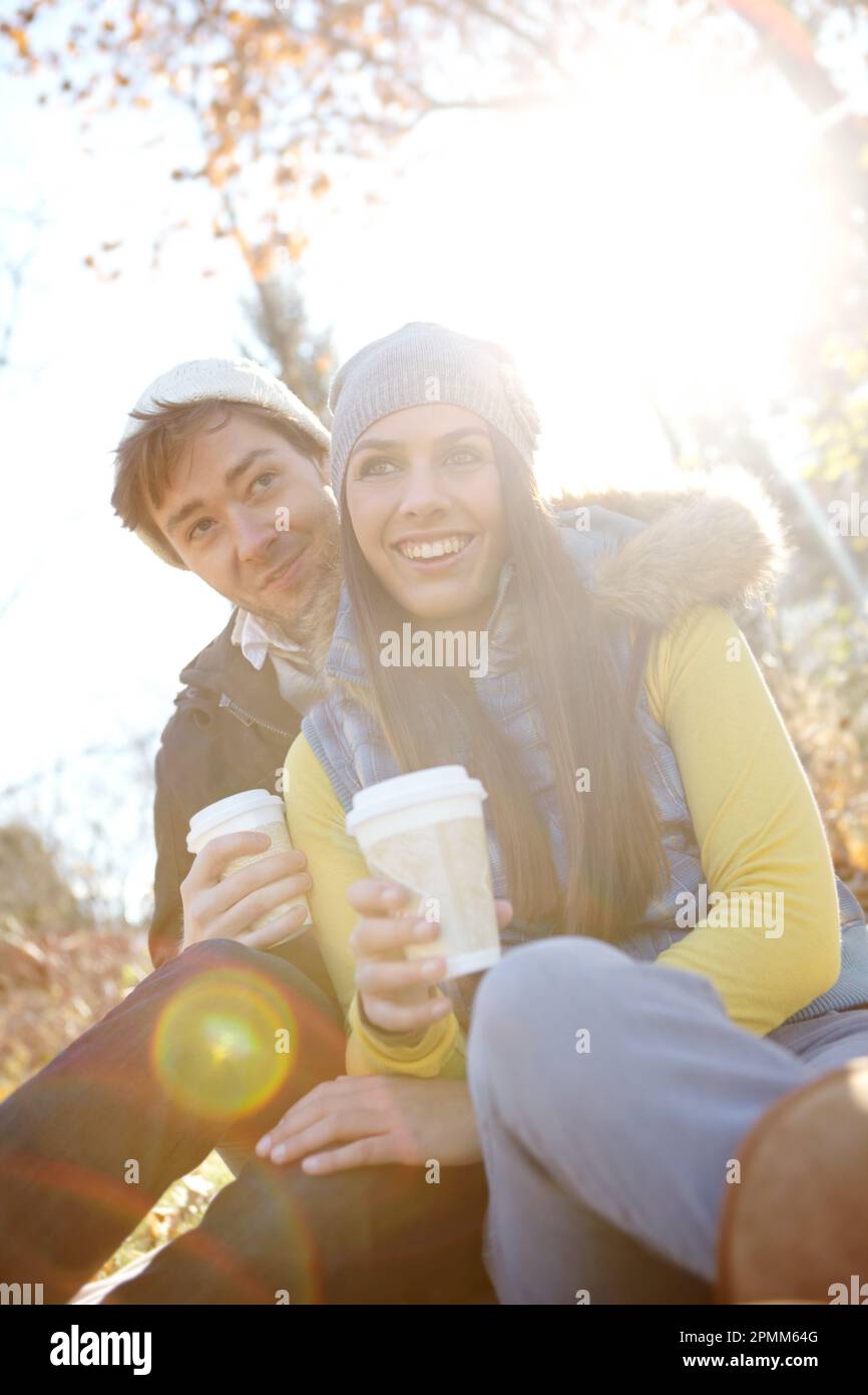 Coffee and cuddles in the outdoors. a loving young couple sitting close ...