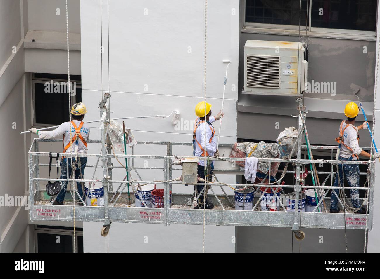 Three workers with safety helmet on scaffold lift painting fresh paint ...