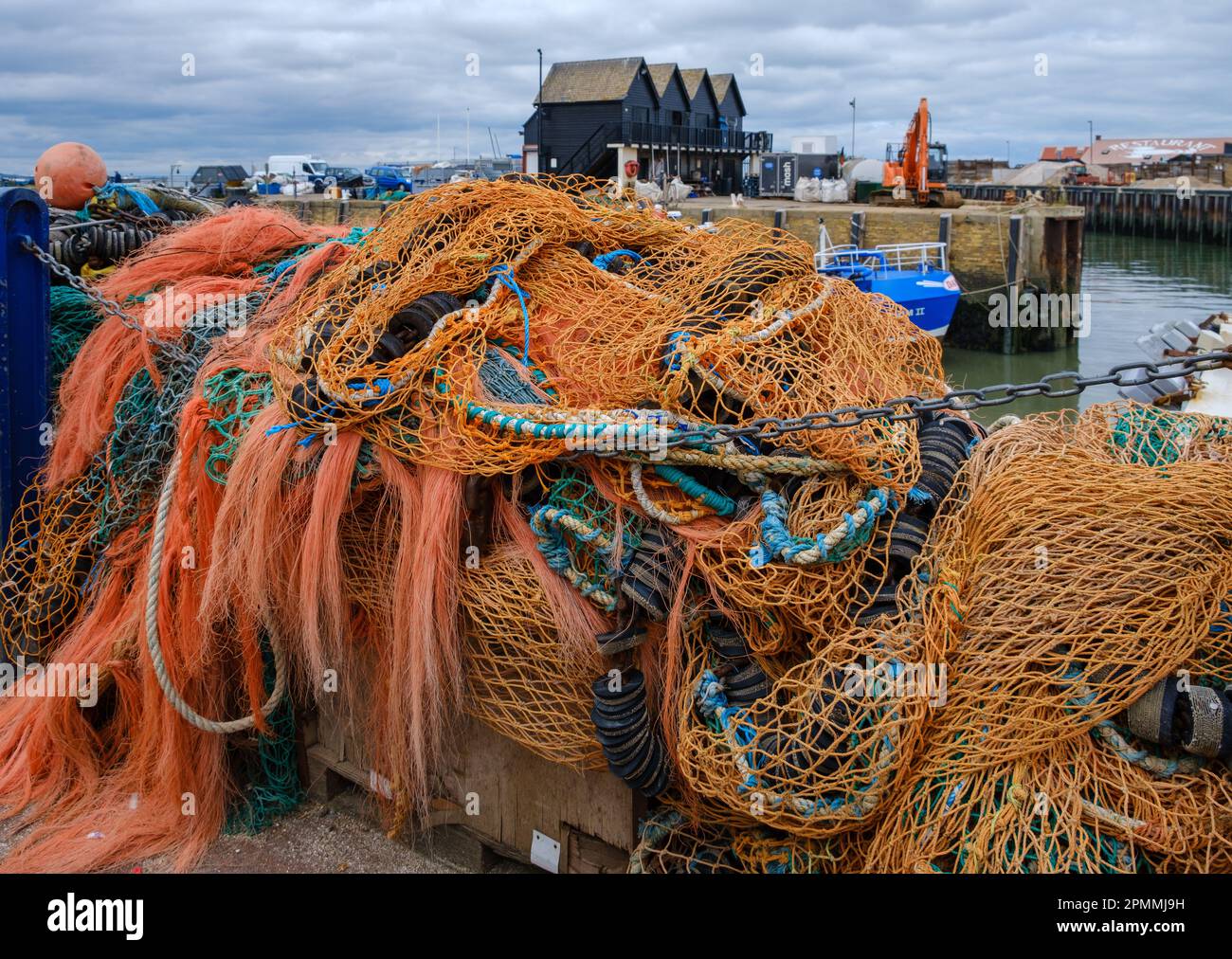 Close-up view of orange fishing nets with wooden huts and fishing boats ...