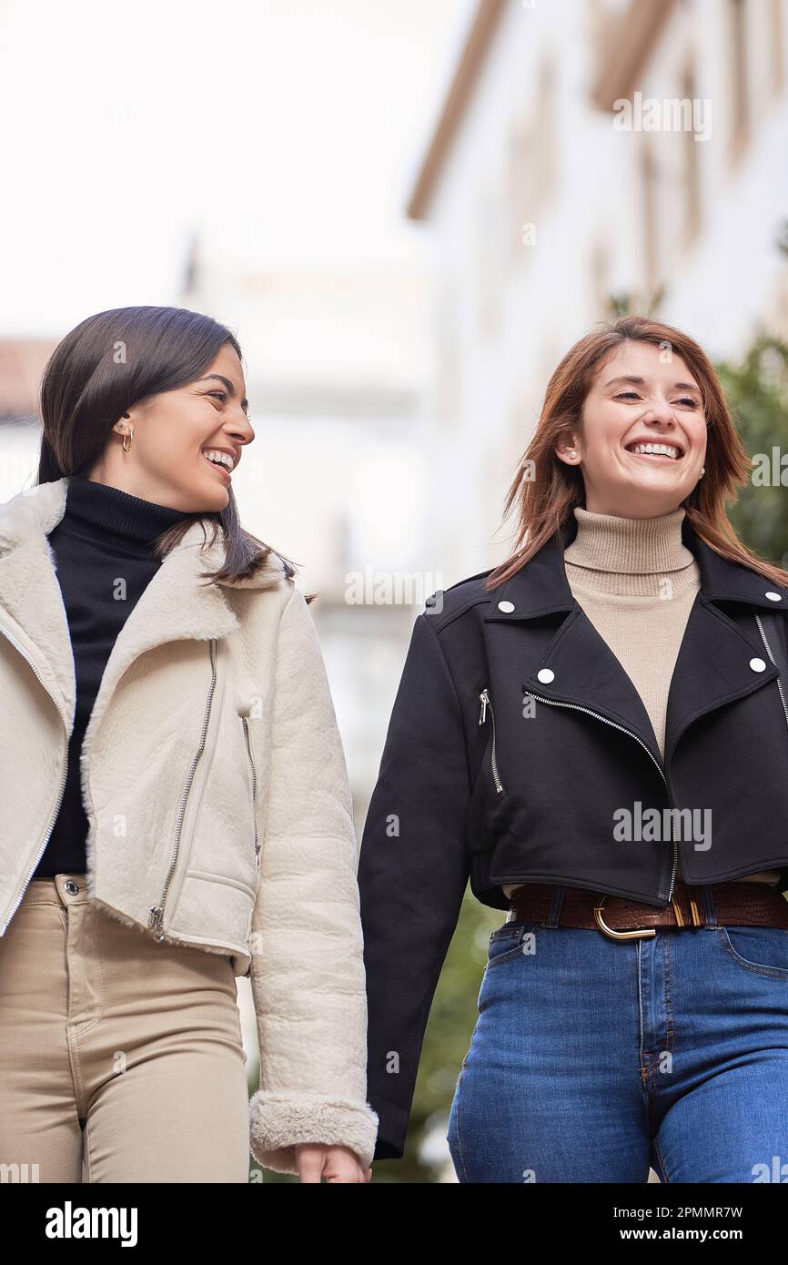 Two happy female friends smiling while walking outdoors together ...