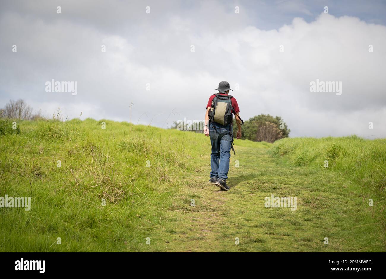 Man walking uphill under a stormy cloudy sky. Long Bay Coastal Walkway ...