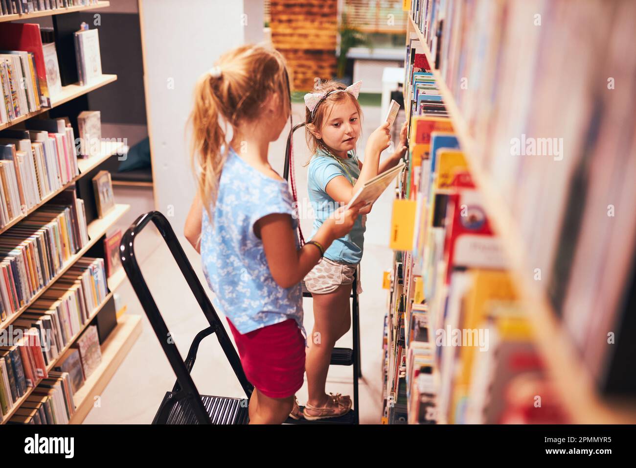 Schoolgirls looking for books in school library. Students choosing set ...