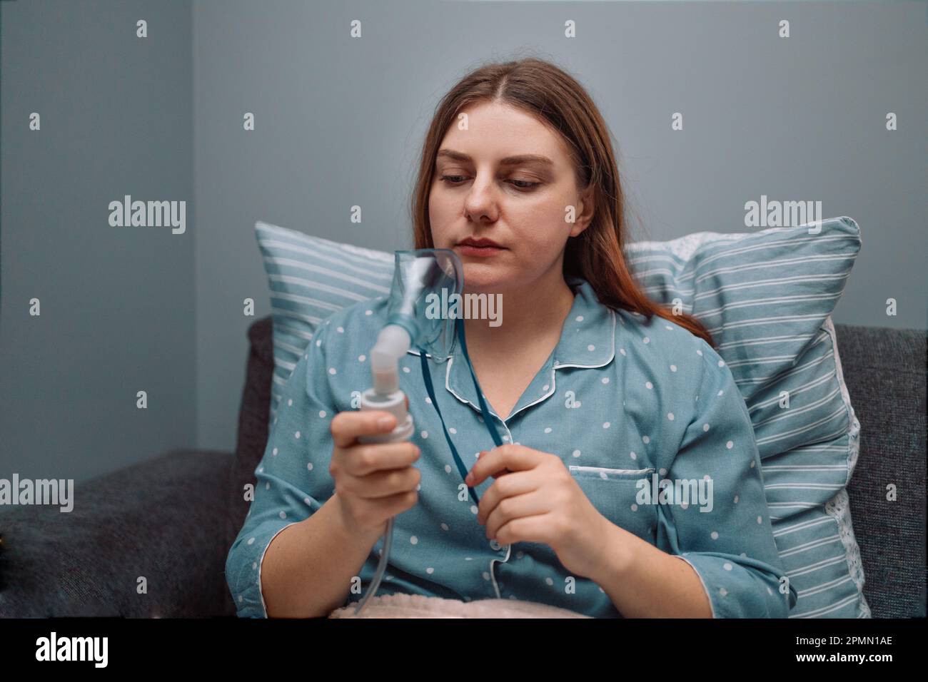 Young sick woman putting on nebulizer mask on face to make inhalation ...
