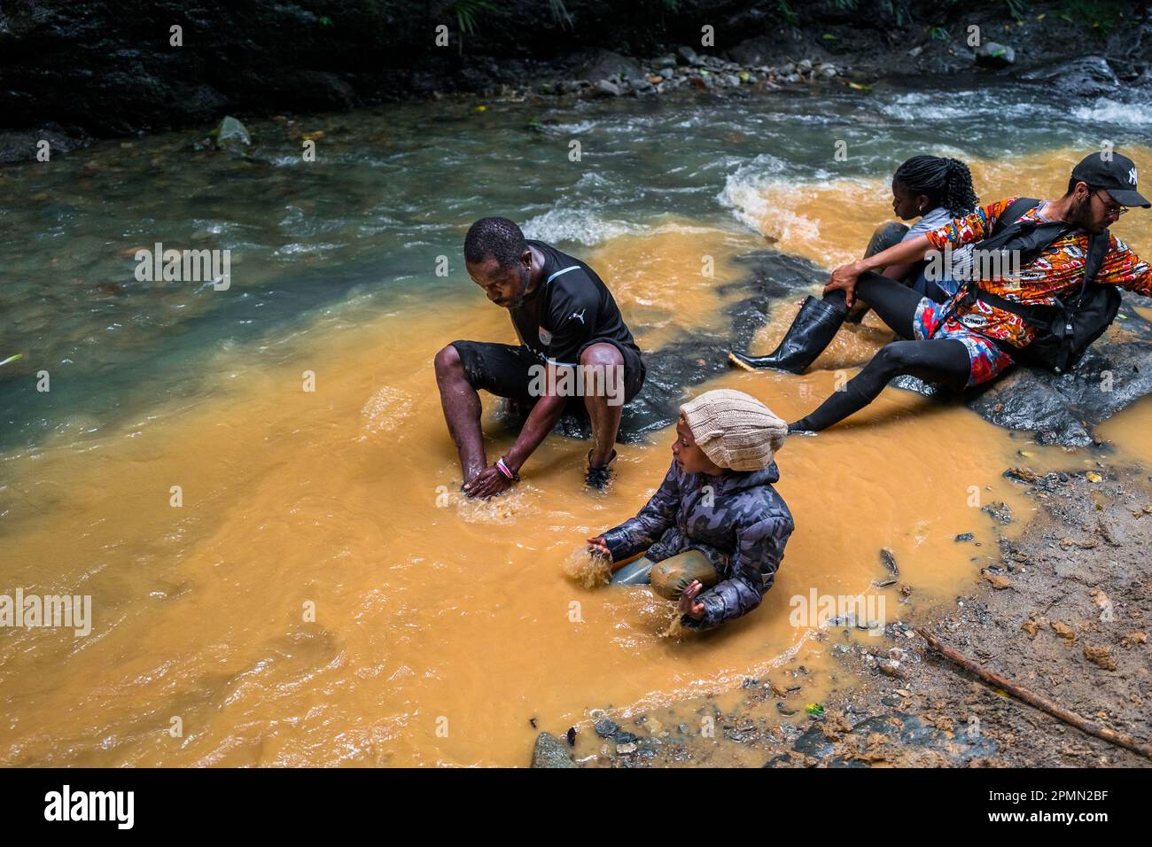 A Nigerian family of migrants washes the mud after passing through a ...