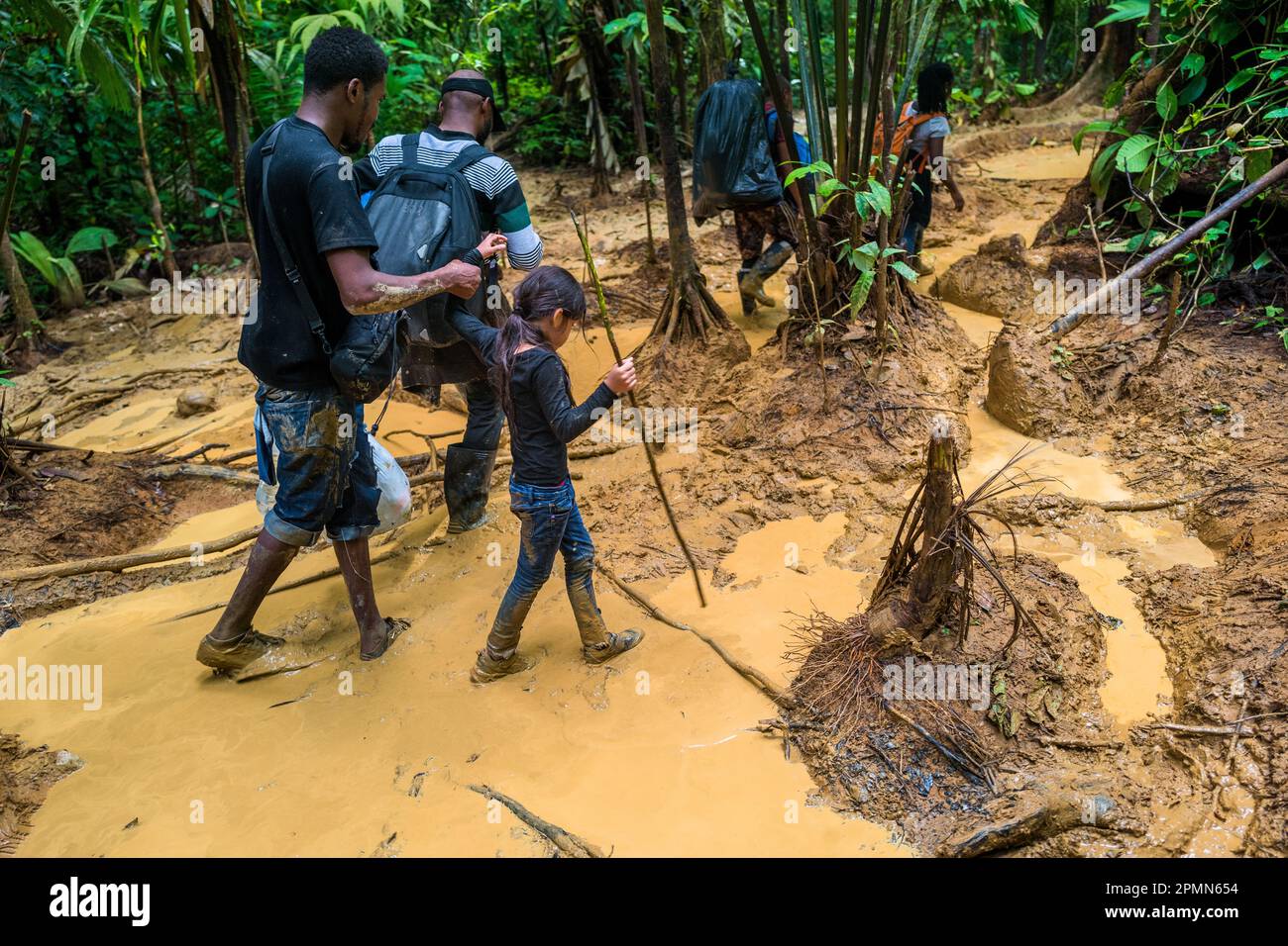 A family of migrants walks through a muddy trail in the wild and ...