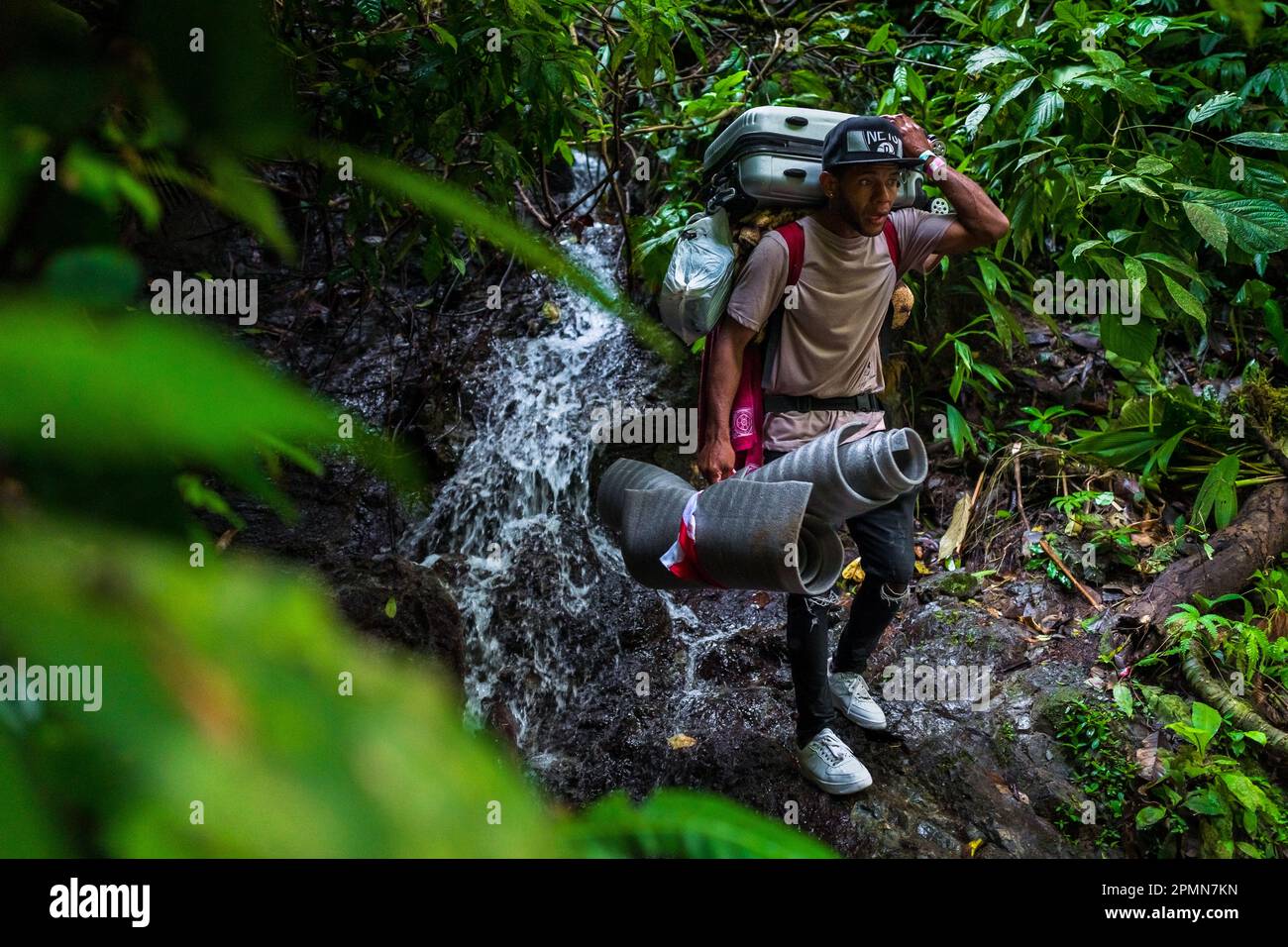 A Venezuelan migrant climbs down a rocky trail alongside a waterfall in ...