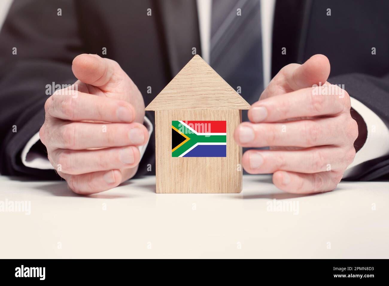 Businessman hand holding wooden home model with South African flag ...