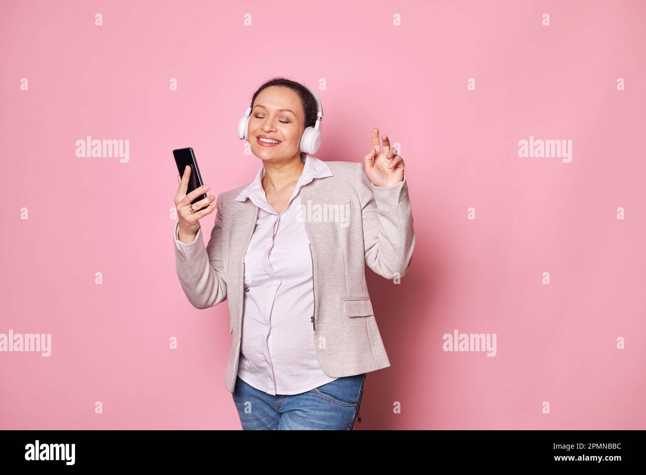 Happy delightful pregnant woman in wireless headphones, holding mobile ...