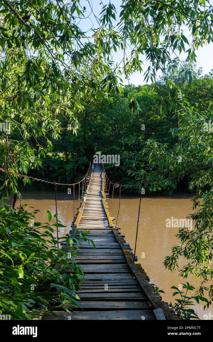 old suspension bridge over the river in the countryside going into ...