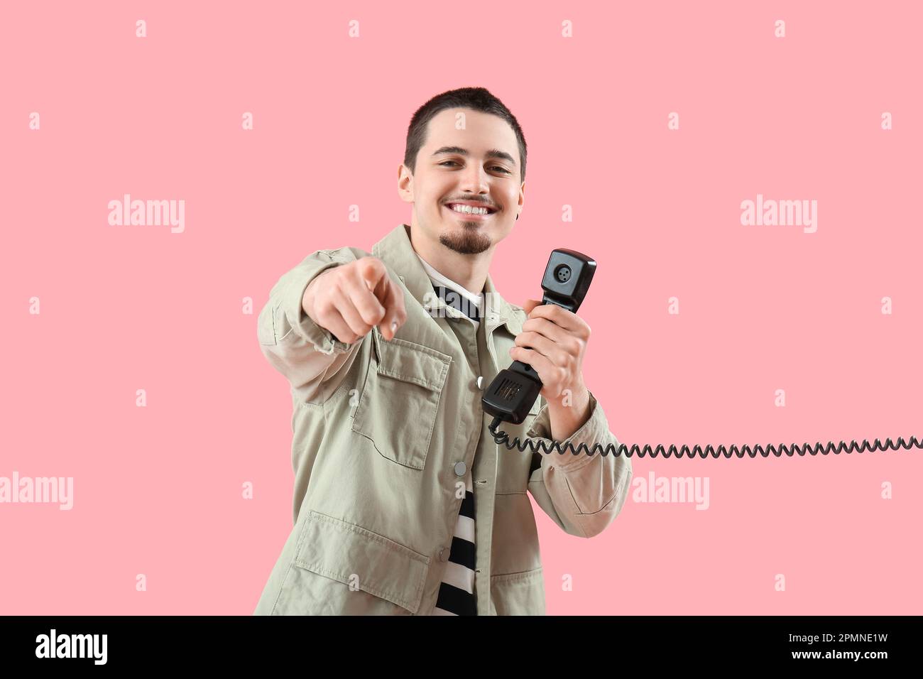 Cool young man with phone receiver pointing at viewer on pink ...