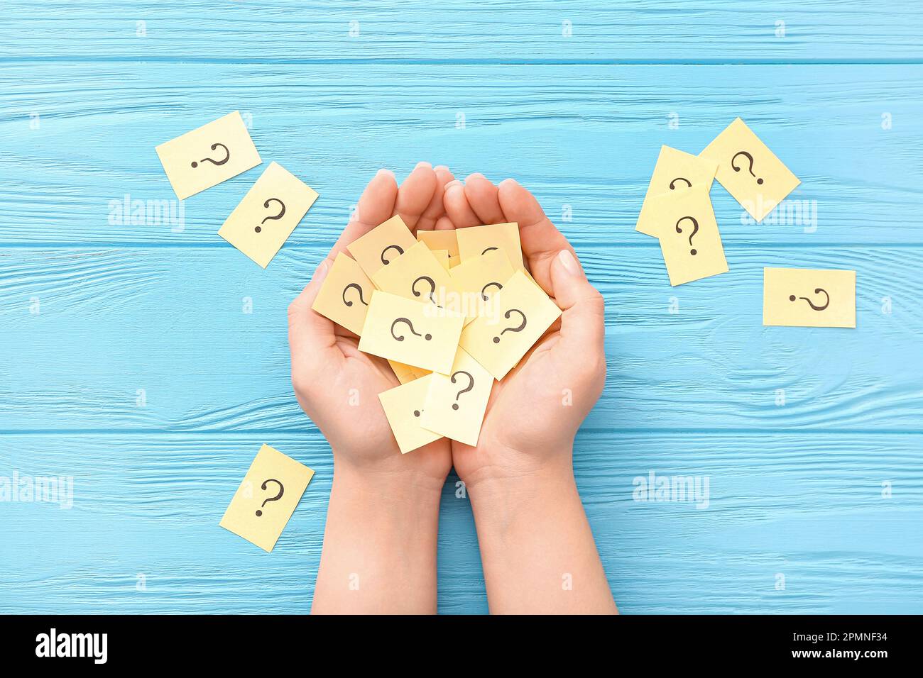 Female hands and papers with question marks on blue wooden background ...