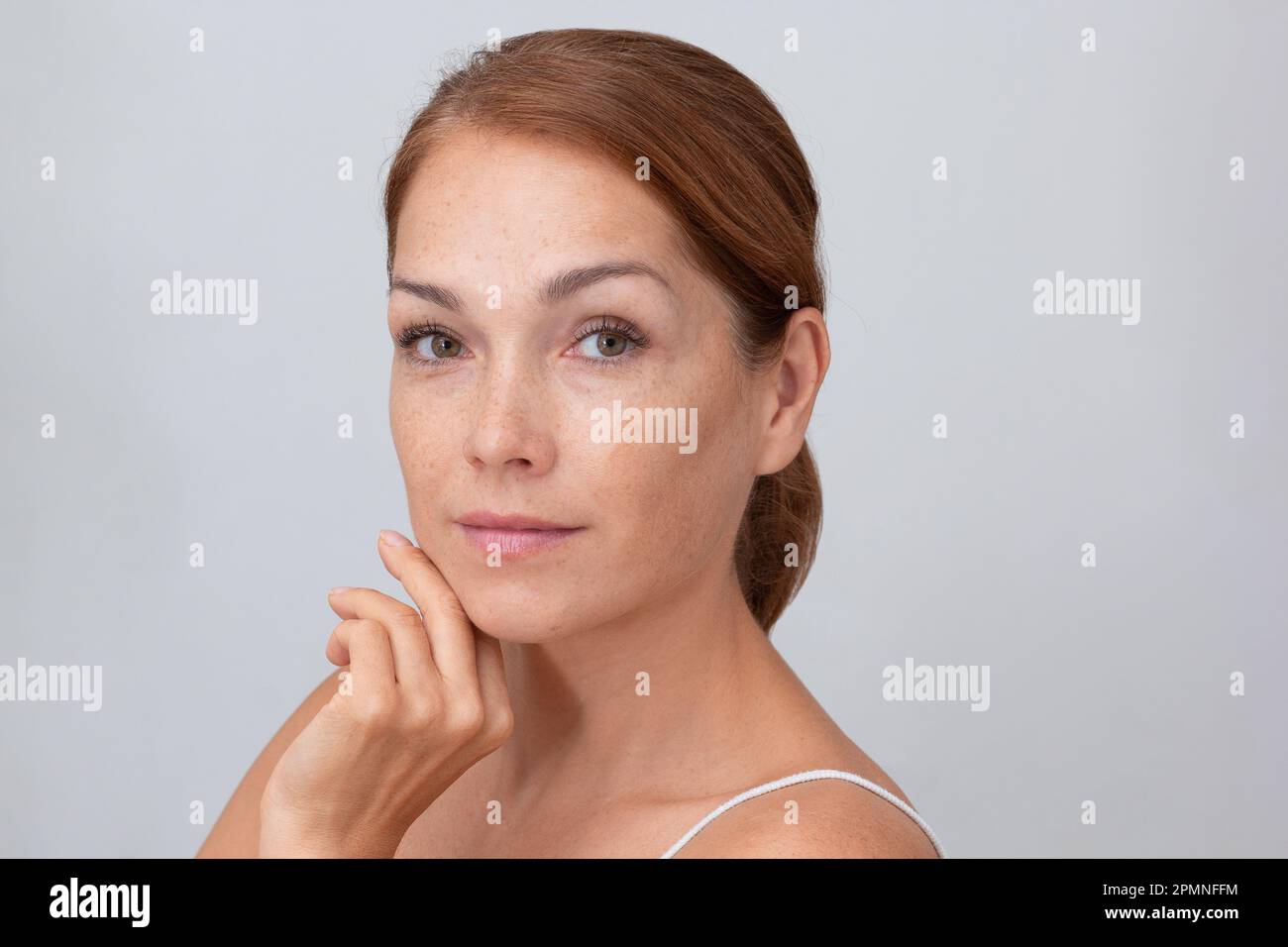 Portrait of cropped caucasian middle aged woman face with freckles holding hand on chin on white ...