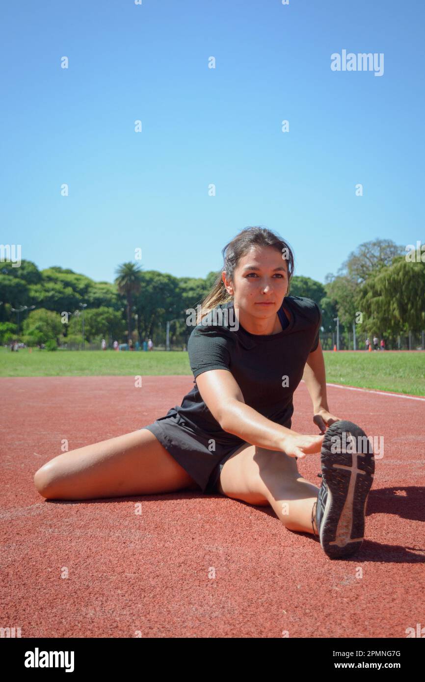 vertical image of young latin woman, stretching leg and hip touching ...