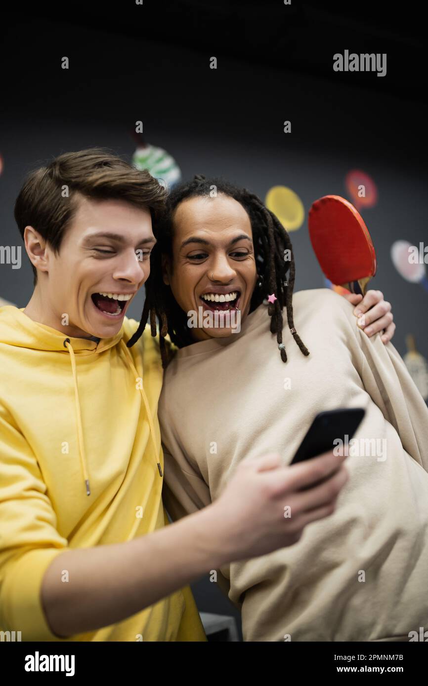 Positive interracial friends with tennis racket using mobile phone in ...