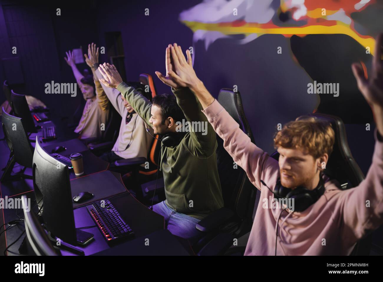 Smiling indian man giving high five to friends near computers in gaming ...