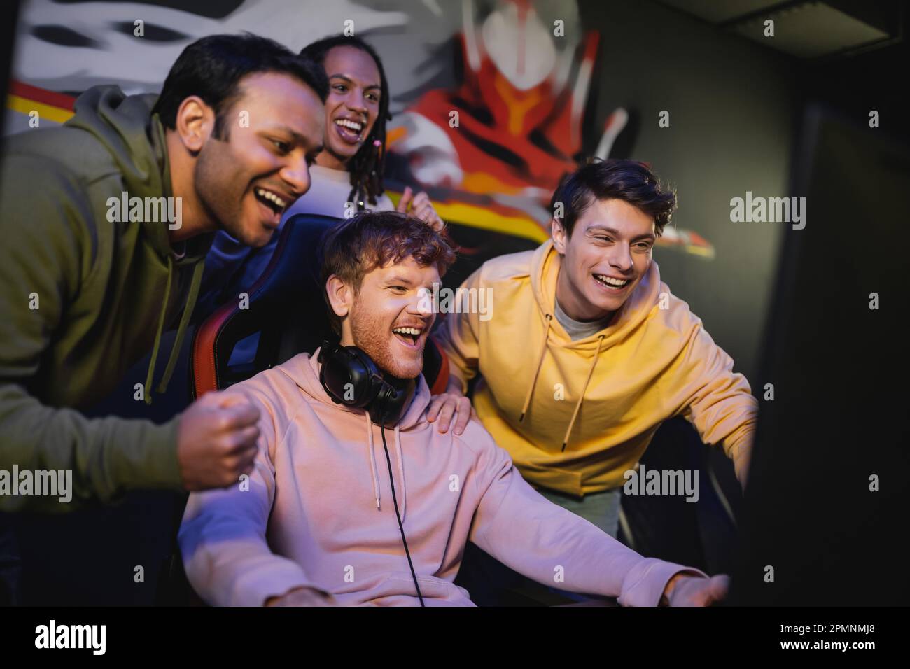 Cheerful multicultural friends playing computer game and rejoicing in ...