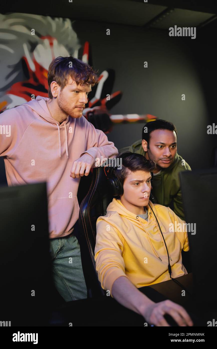 Focused multiethnic team playing video game on computer in gaming club ...