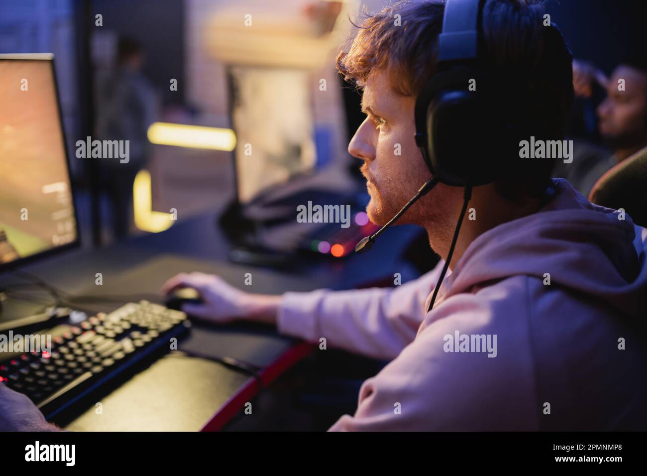 Side view of focused gamer in headphones playing video game on computer ...