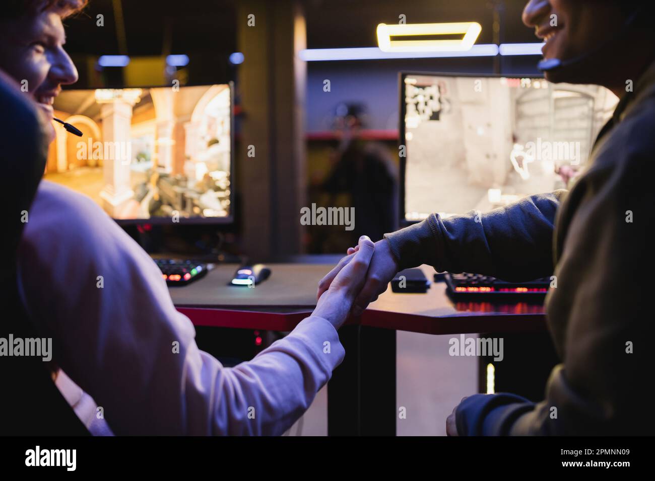 Positive gamers shaking hands near blurred computers in gaming club ...