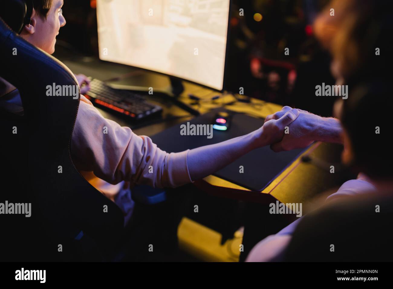 Gamers shaking hands while playing computer game in cyber club,stock ...