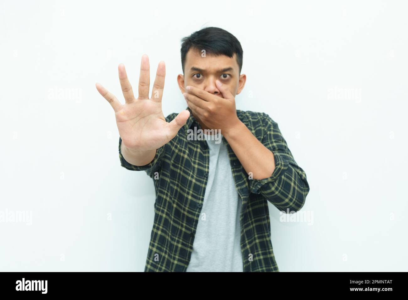 Young Asian man facing his palms forward while covering his mouth as a ...