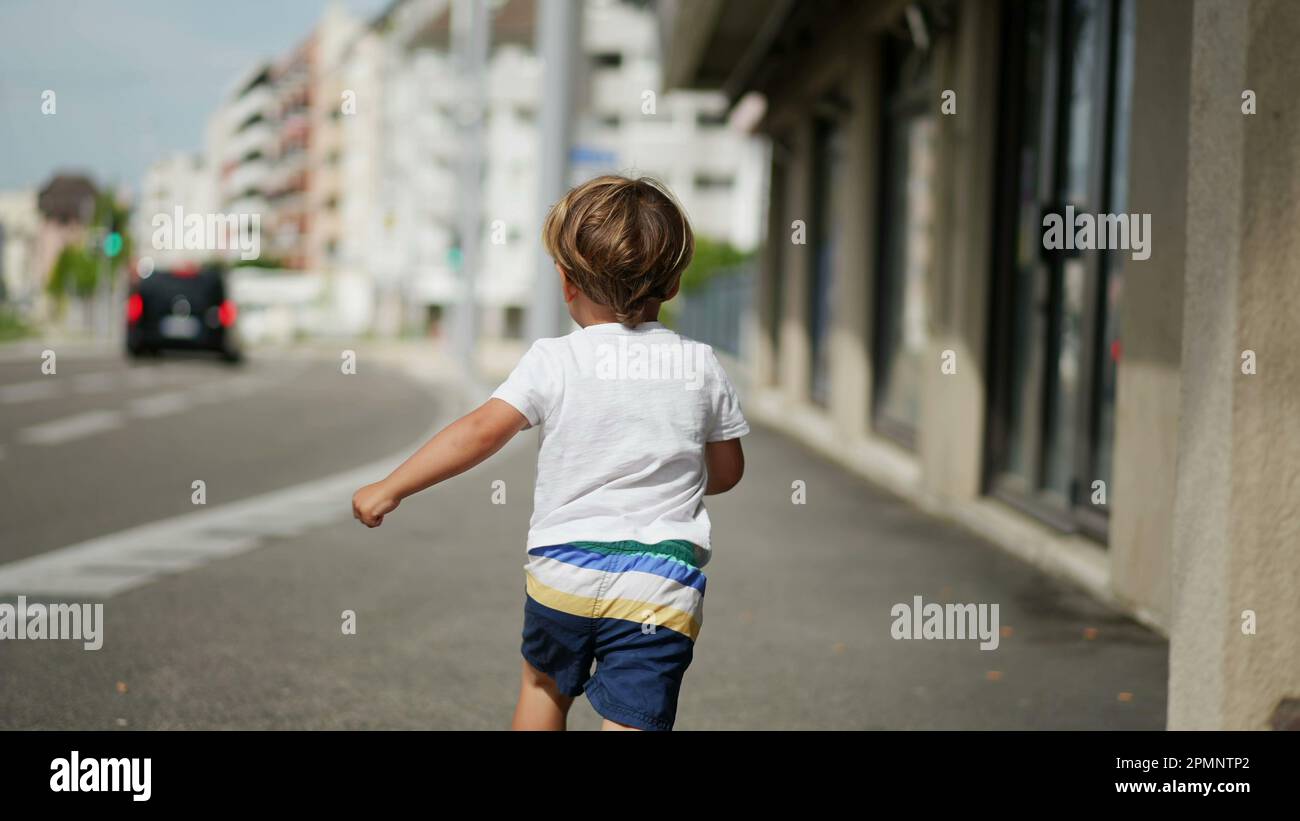 Back of child running outside in city street. Little boy runner ...