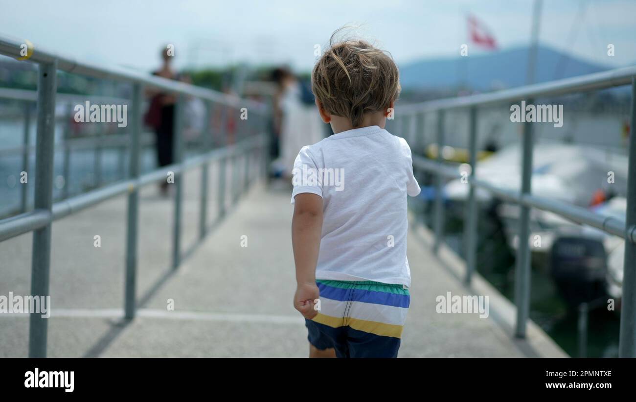 Back of one little boy running outside at bridge during summer day ...