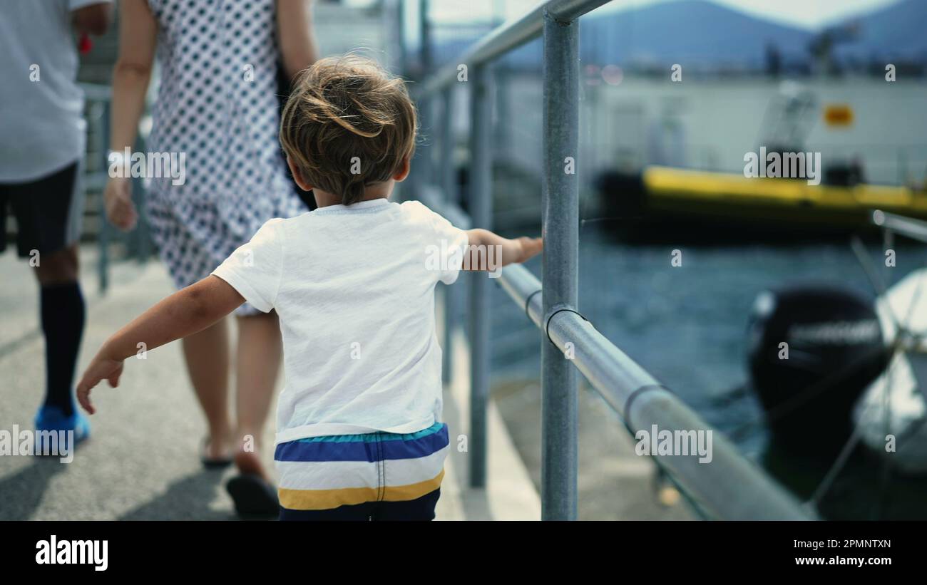 Child holding on metal rail crosses bridge outdoors in sunny day. Back ...