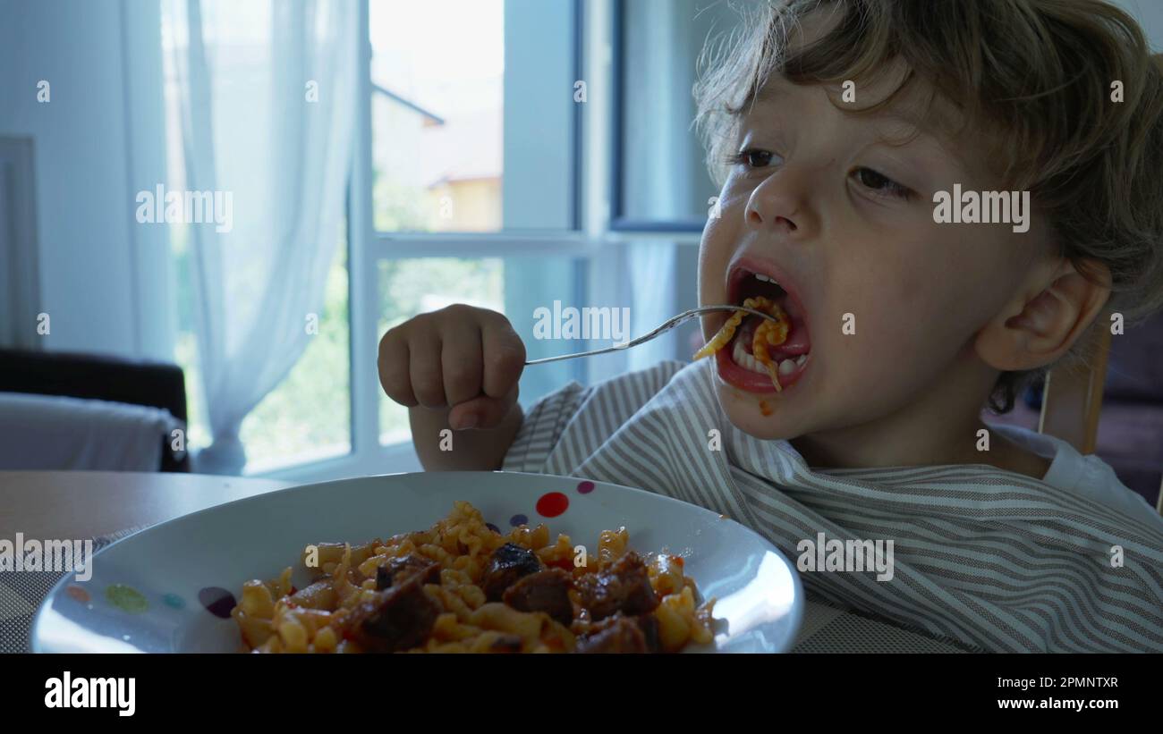 Child eating pasta food for lunch at home. Authentic lifestyle scene of ...