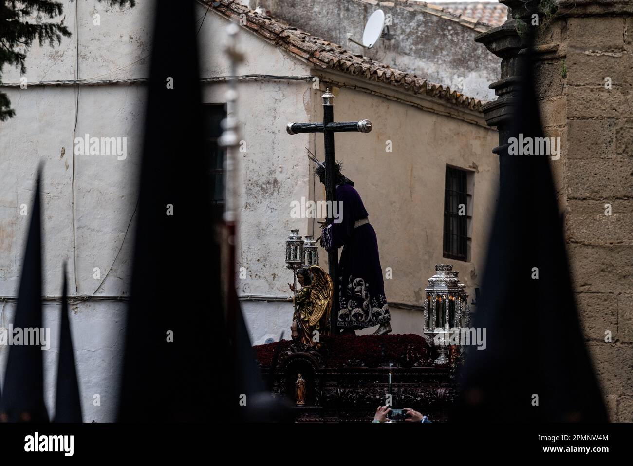 The black cone shaped hoods of penitents frame a statue of Jesus with ...