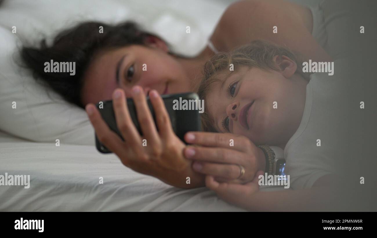 Mom and child looking at phone device together lying in bed. Candid ...